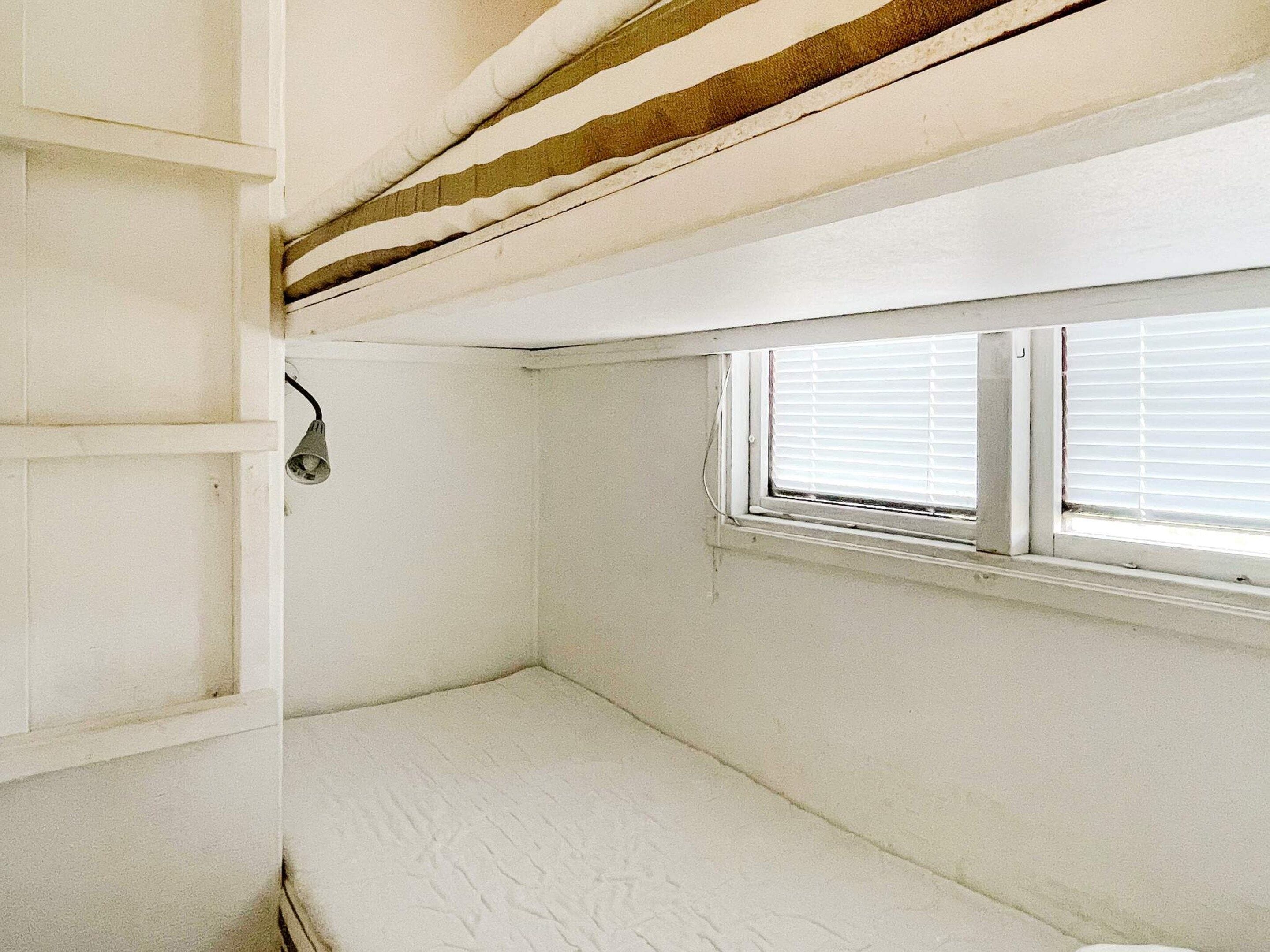 Quarto pequeno com cama de solteiro, janela e uma viga no teto aparente.
