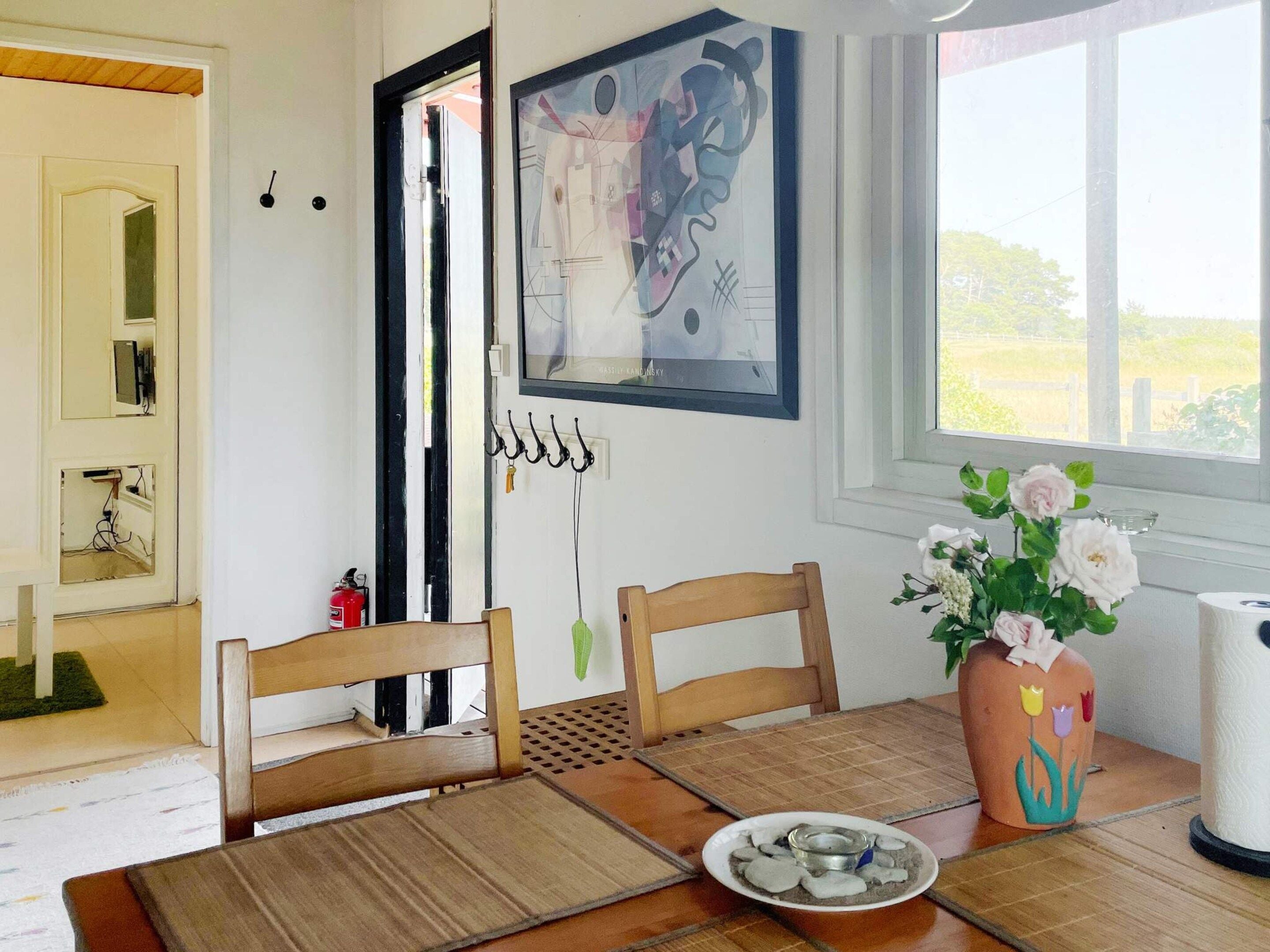 Uma área de refeições com mesa, cadeiras, um vaso com flores e uma obra de arte na parede.