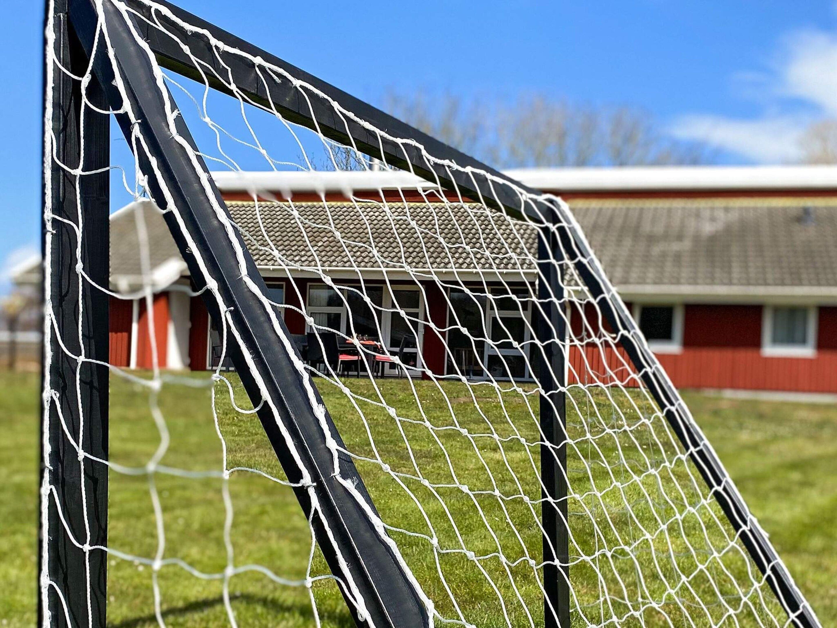 Um gol de futebol com rede, em um campo de grama com um edifício ao fundo.