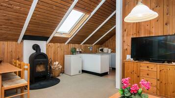 Uma cabana acolhedora com interior de madeira, lareira, televisão e área de jantar.