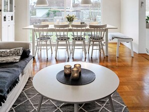 Uma sala de estar moderna com uma mesa de centro redonda, mesa de jantar branca e cadeiras.