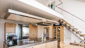 Cozinha moderna com ilha central, eletrodomésticos de aço inoxidável, armários de madeira e área de jantar com mesa e cadeiras de madeira.