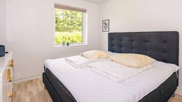 Quarto com cama, janela, uma pequena planta e um quadro na parede.