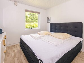 Quarto com cama, janela, uma pequena planta e um quadro na parede.