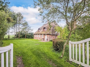 Uma casa com telhado de palha e fachada de tijolos, rodeada por um gramado e árvores.