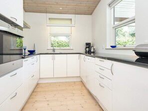 Cozinha moderna com armários brancos, piso de madeira e janela com persianas.