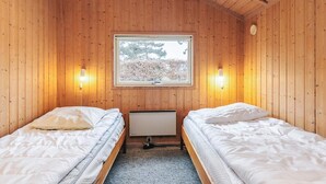 Quarto de cabana de madeira com duas camas, uma janela e luminárias fixadas na parede.