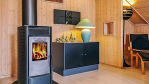Um quarto acolhedor com uma lareira a lenha, um armário com objetos decorativos, um abajur e uma poltrona.