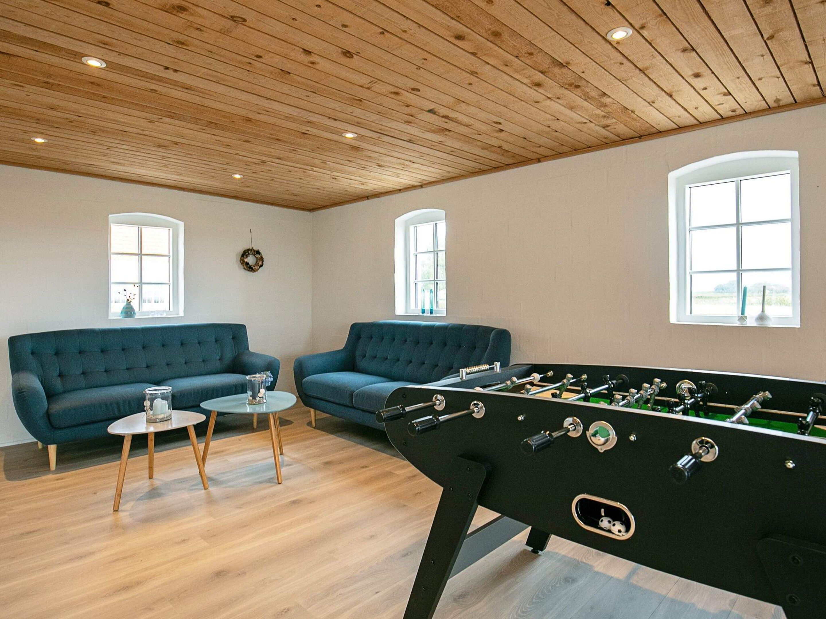 Quarto com mesa de futebol, dois sofás, uma mesa redonda pequena e duas janelas.