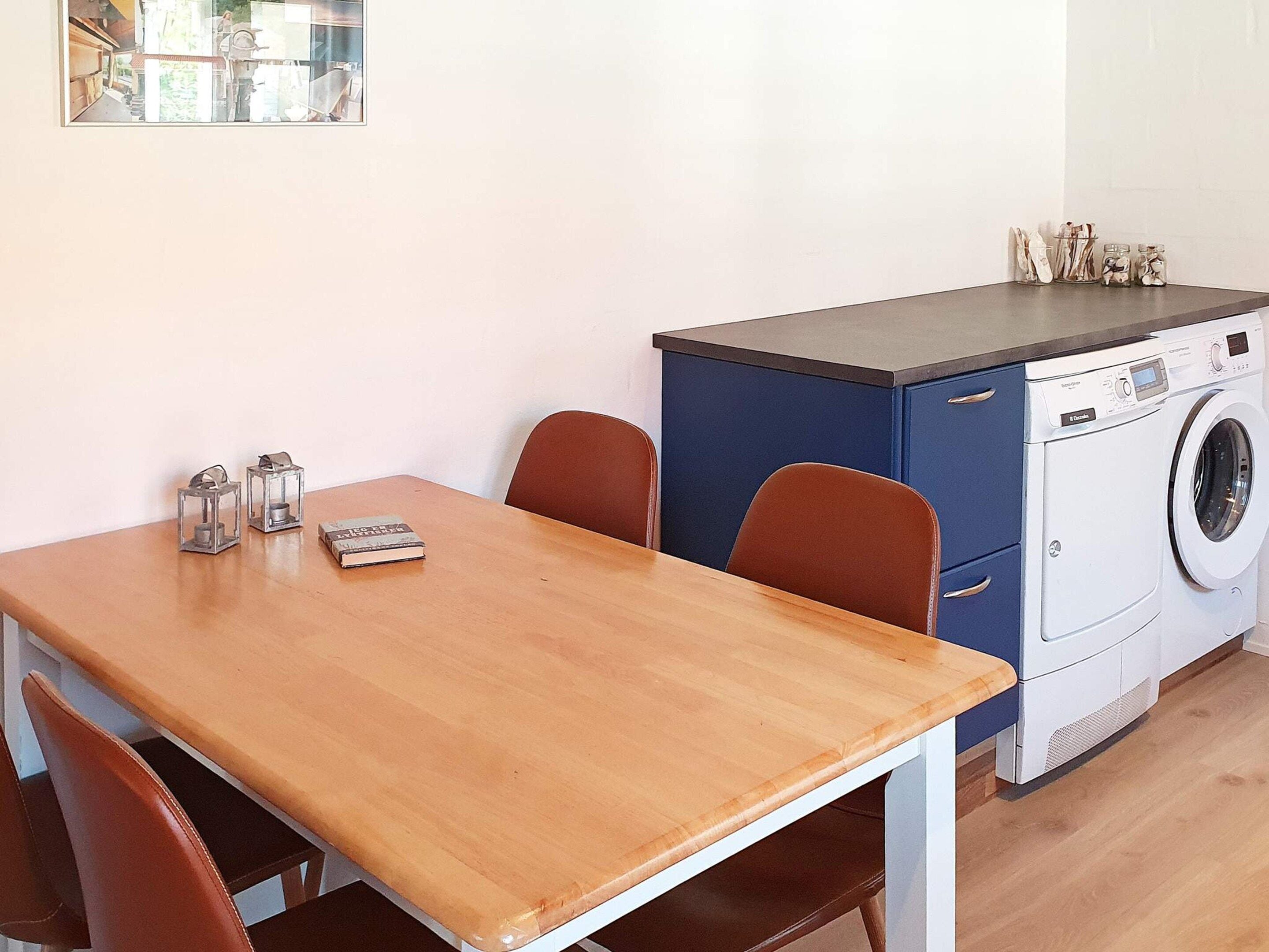 Cozinha compacta com máquina de lavar, mesa de jantar com cadeiras e um pequeno armário.
