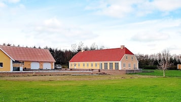 Um edifício de dois andares com telhado vermelho e paredes amarelas, ao lado de um campo verde.