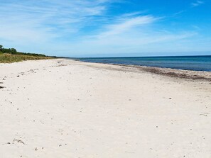Uma extensa praia de areia com céu claro e mar calmo.