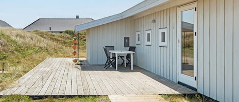 Um edifício moderno com deck de madeira, mesa e cadeiras, e porta com janelas.