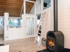 Um interior moderno com lareira a lenha, um espaço de cozinha no mezanino e uma escada de madeira.