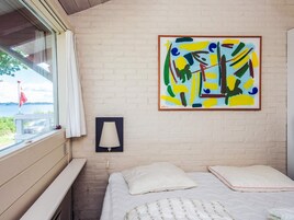 Quarto com cama, janela com cortinas, luminária na parede e pintura abstrata colorida.