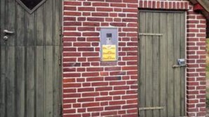 Uma parede de tijolos com duas portas de madeira, uma delas com uma placa.