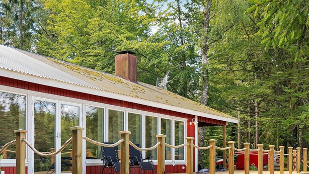 Um deck de madeira com uma barreira de corda, um edifício vermelho com grandes janelas e um fundo arborizado.