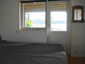 Um quarto com uma cama, uma janela com vista para o exterior e um espelho fixado na parede.