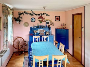 Um quarto com uma mesa de jantar, cadeiras, um armário azul, um fuso de fiar e uma porta.