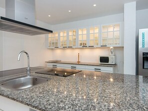 Cozinha moderna com bancadas de granito, eletrodomésticos de aço inoxidável e armários brancos.