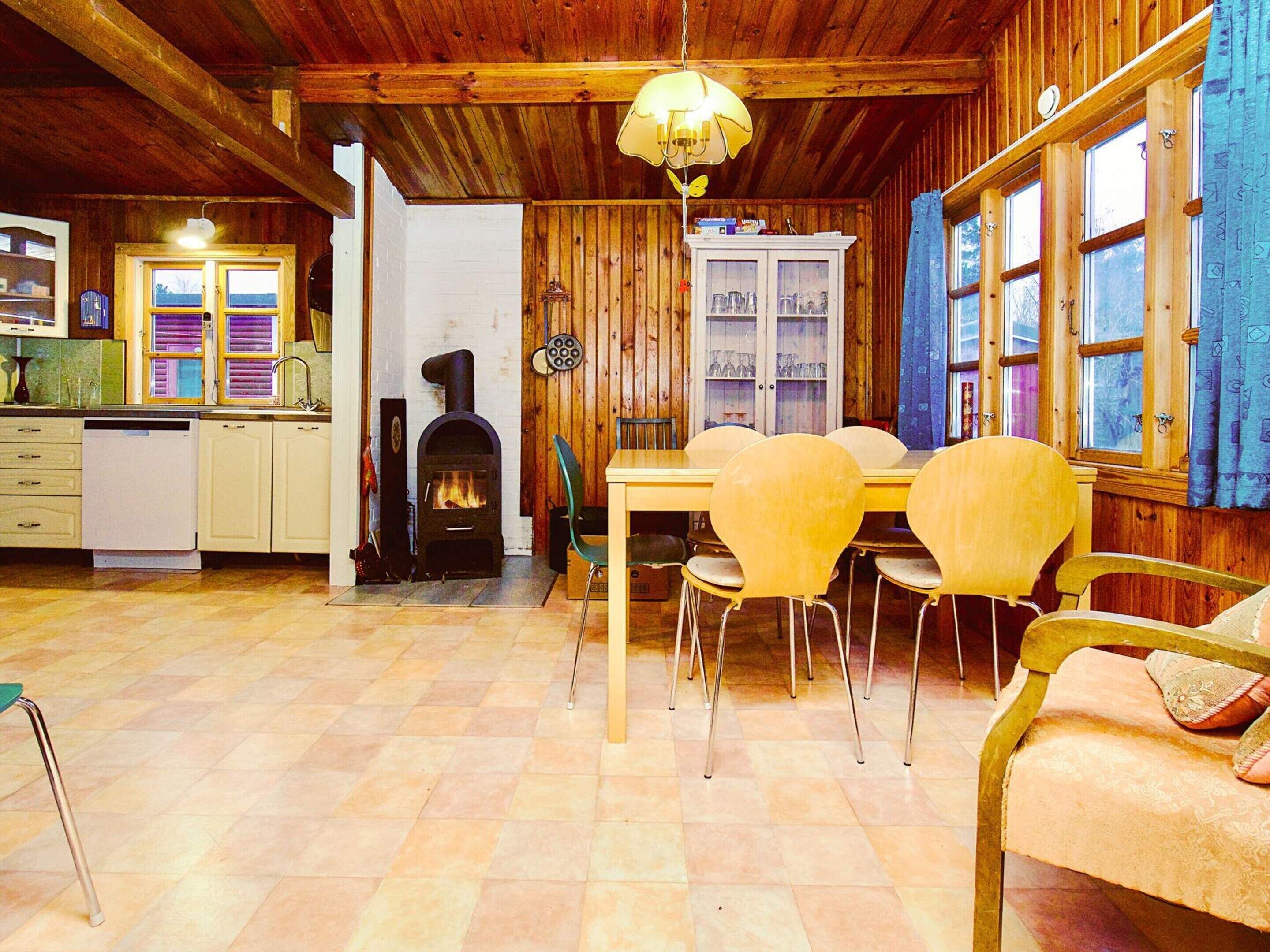 Interior acolhedor de uma cabana com mesa de jantar de madeira, cadeiras, lareira e área de cozinha com armários e pia.