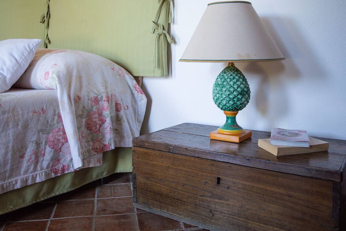Quarto com cama, mesa de cabeceira, abajur e um livro.