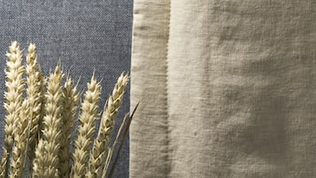 Primeiro plano de um tecido com textura, possivelmente para estofados de sofá ou poltrona, ao lado de um tecido liso e claro.
