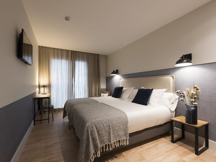 Quarto moderno com uma cama grande, mesas de cabeceira, escrivaninha e televisão presa à parede.