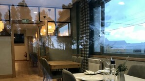 Uma área de refeições com uma mesa posta para dois, vista do exterior e um aviso indicando uma saída de emergência.