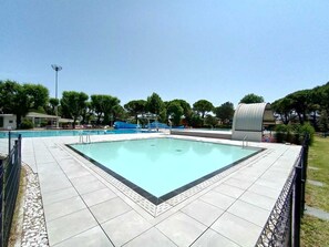 Piscina retangular com deck revestido e cercada por grade de metal.
