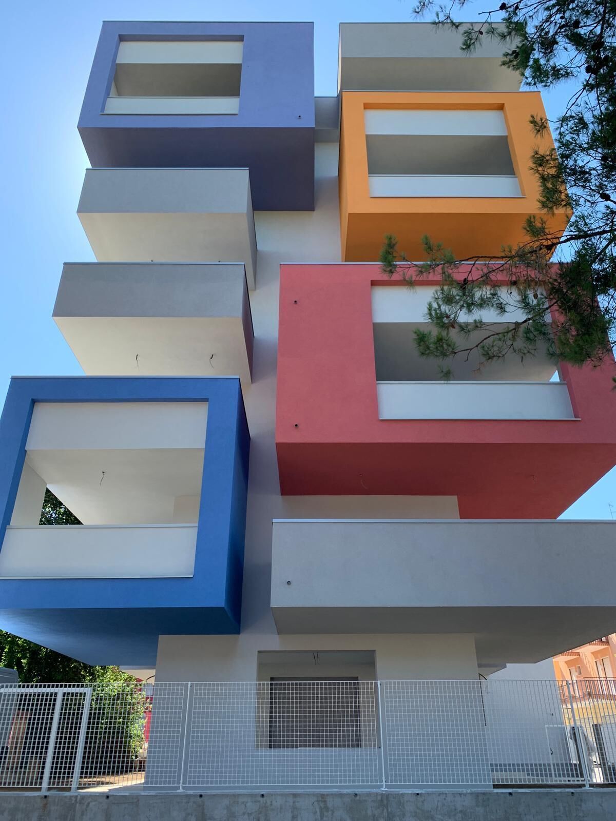Um edifício com vários andares e varandas geométricas em azul, laranja e vermelho.