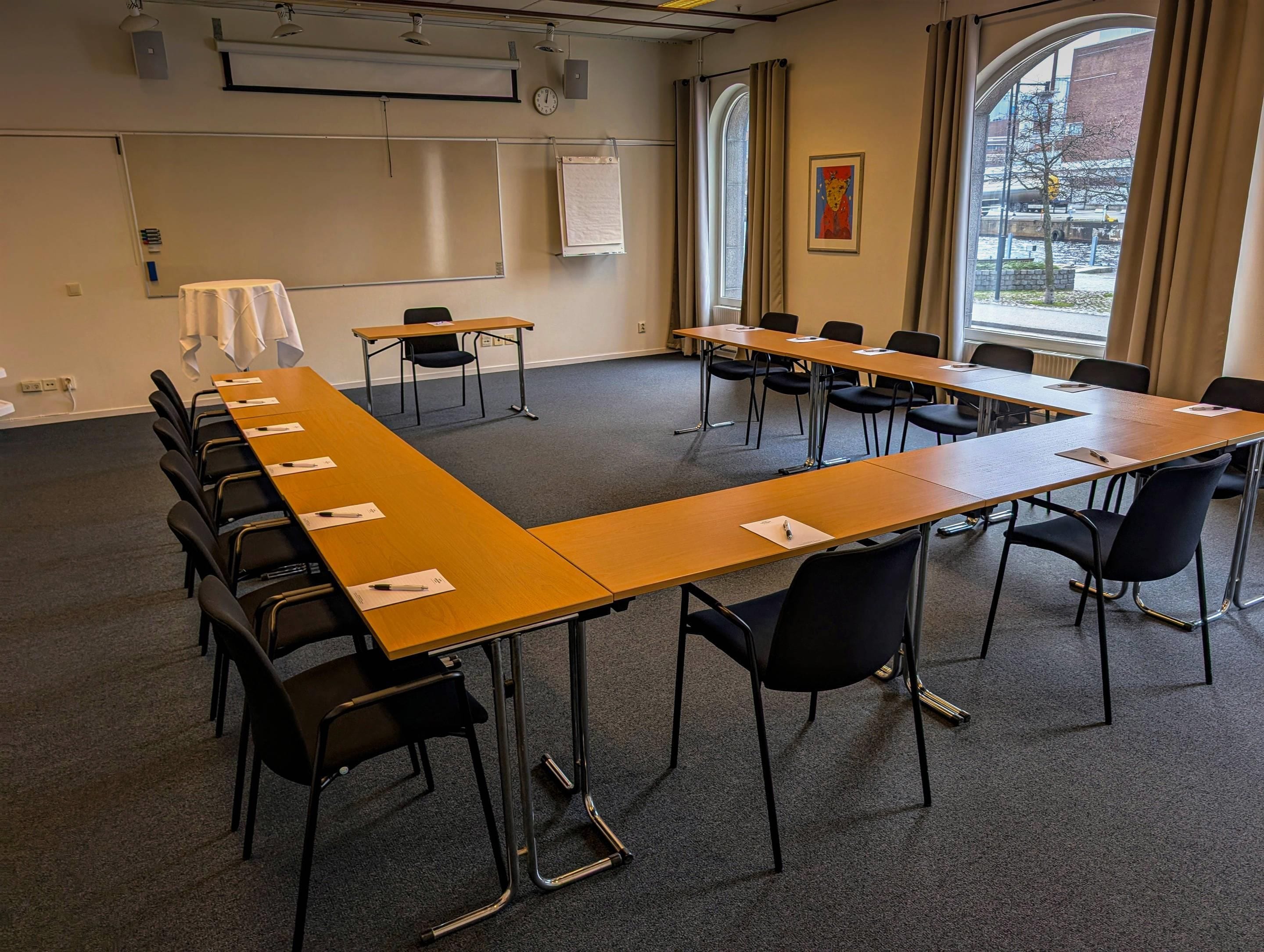 Sala de conferências com uma mesa comprida, cadeiras, tela de projetor e janela com cortinas.