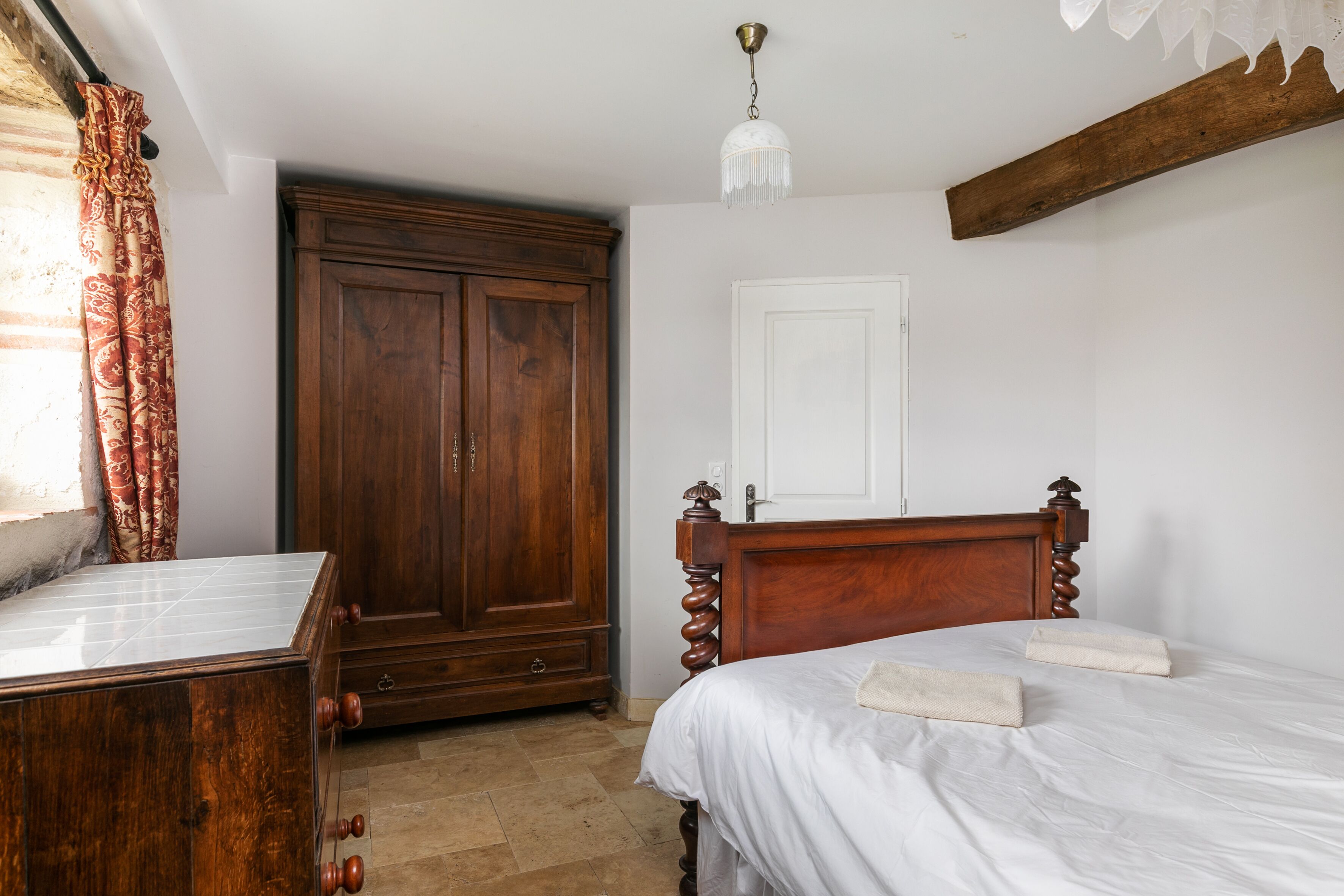 Quarto com guarda-roupa de madeira, cama com roupa de cama branca e luminária pendente.