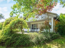 Uma casa moderna com varanda coberta, rodeada por vegetação exuberante e árvores.