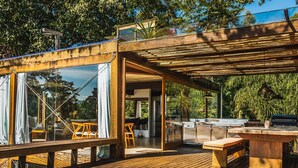 Uma cozinha externa moderna com deck de madeira, mesa de jantar e churrasqueira.