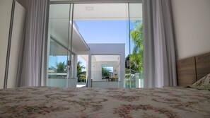 Quarto com uma cama grande, vista para uma sala de jantar e uma porta de vidro deslizante que dá para uma varanda.