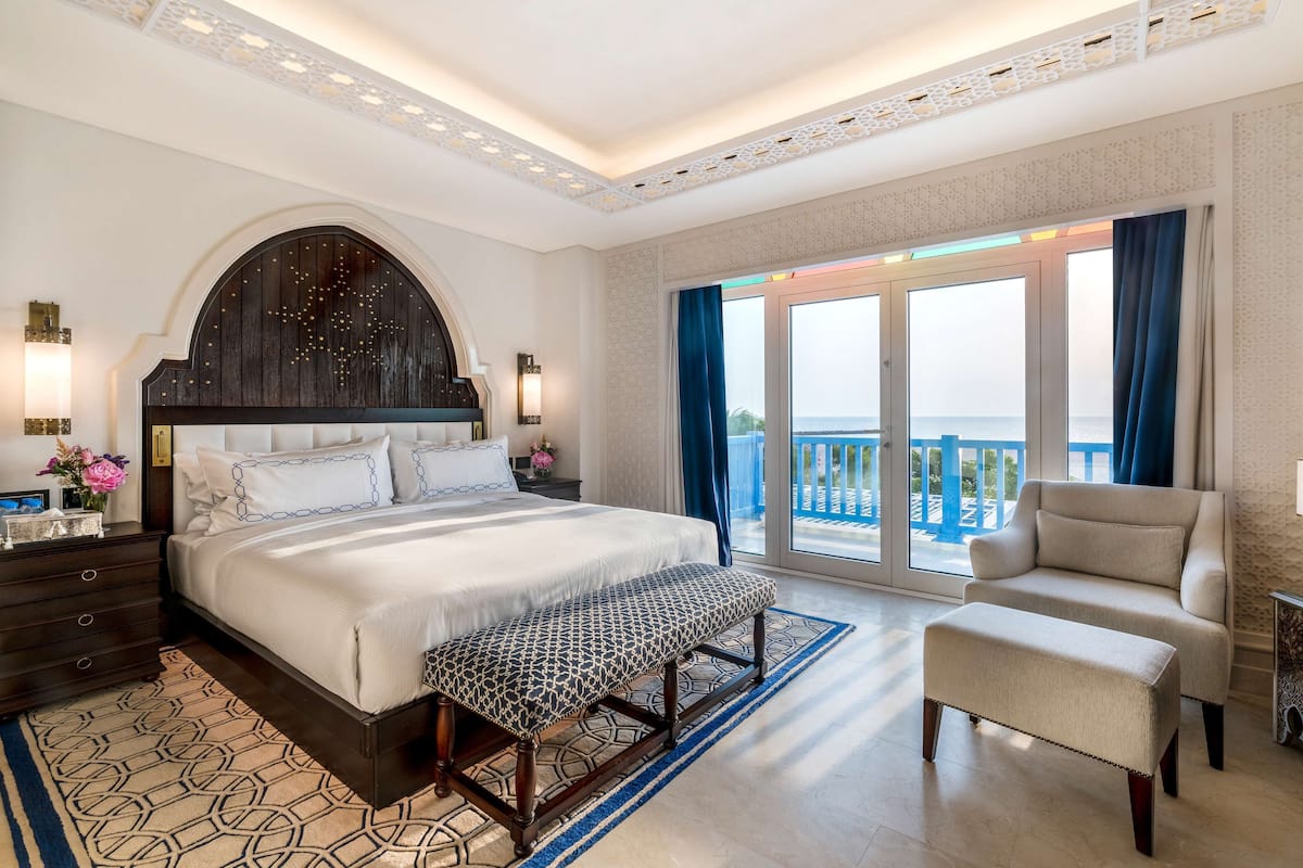 Quarto espaçoso com cama grande, um banco, uma cadeira e varanda com vista.