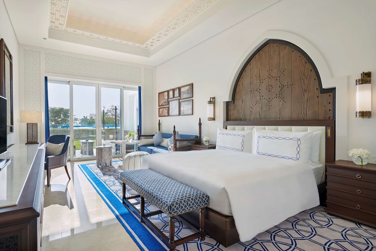 Quarto de hotel espaçoso com uma cama grande, televisão, área de estar com um banco e vista para o exterior.