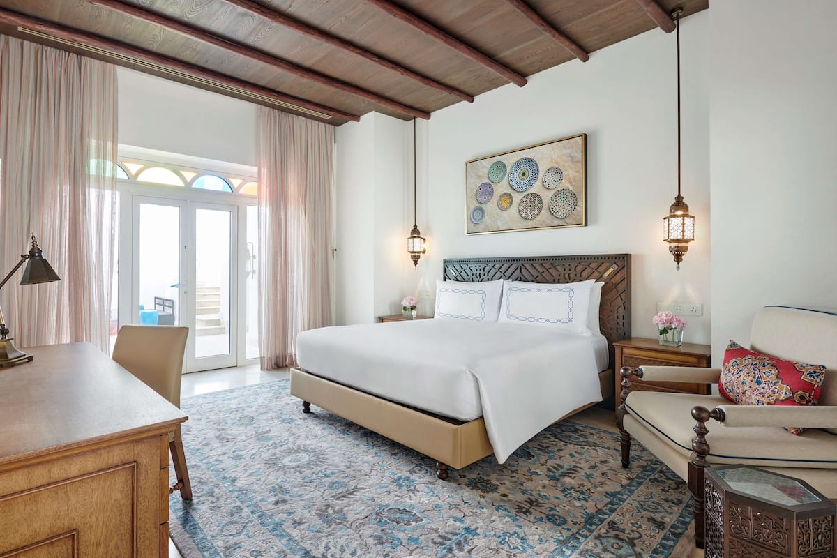 Quarto de hotel com uma cama grande, uma escrivaninha, uma cadeira e vista para o exterior.