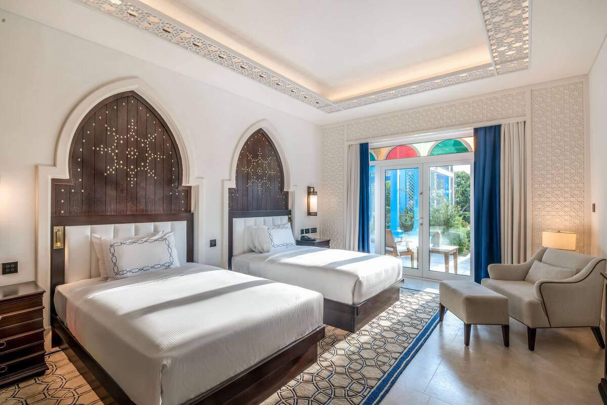 Quarto de hotel com duas camas, um sofá e vista para o exterior.