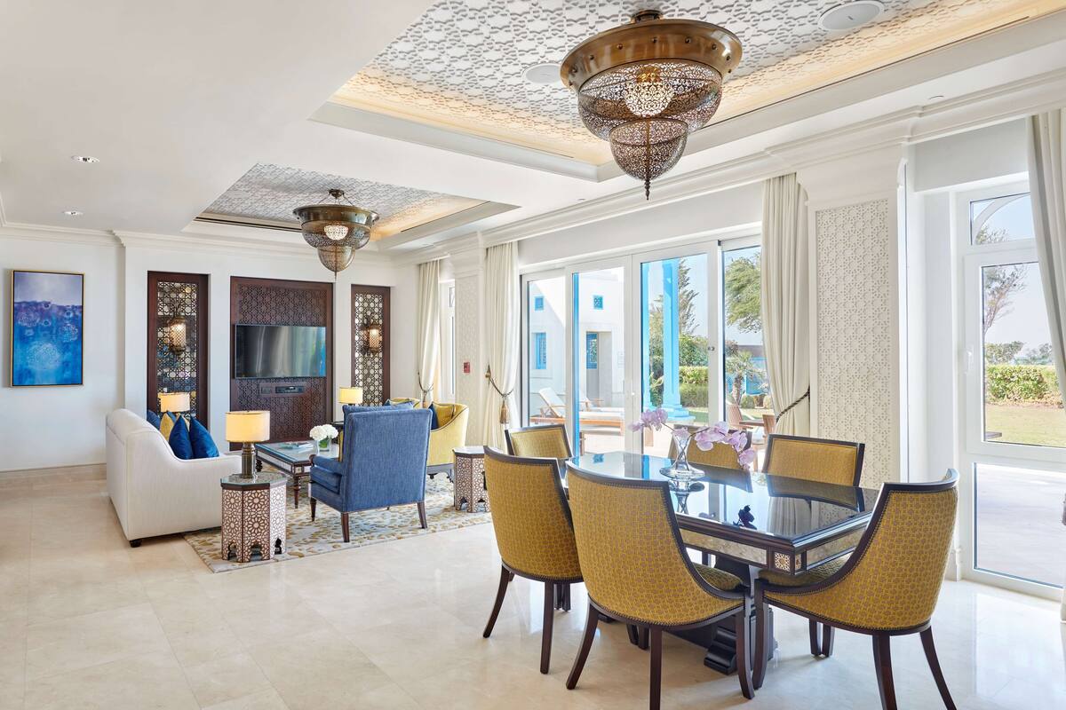 Ampla sala de estar com um sofá moderno, uma mesa de jantar com cadeiras e uma grande janela com vista para o exterior.