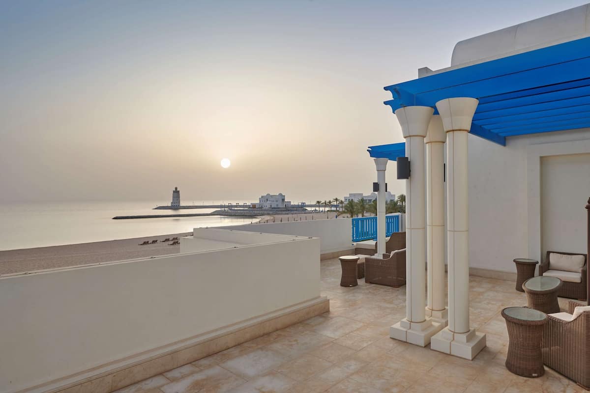 Terraço no telhado com vista para o mar, com área de estar ao ar livre e toldo azul.