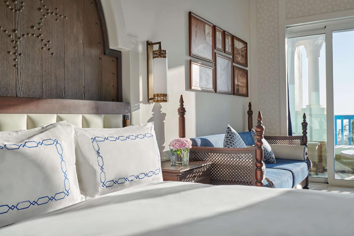 Quarto de hotel com cama, cabeceira de madeira, mesa de cabeceira com um vaso de flores e varanda com vista.