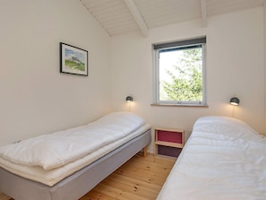 Quarto com duas camas de solteiro, janela com vista para árvores e quadro na parede.