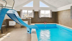 Uma piscina com escorrega azul, uma janela com cortinas e uma toalha no peitoril.
