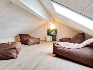 Um quarto de sótão acolhedor, com teto inclinado, piso de madeira e uma televisão sobre um armário branco.