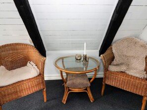 Quarto de canto com duas cadeiras de vime, uma mesa de vidro e um banquinho.