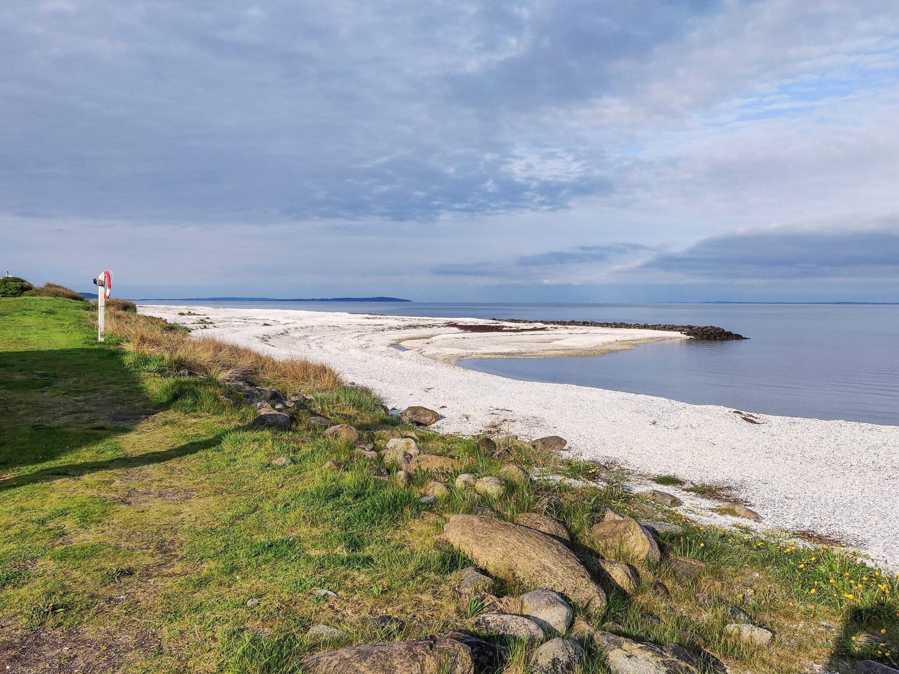 Paisagem costeira com praia de pedras, áreas com grama e um sinalizador.
