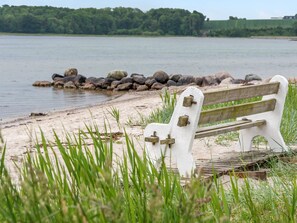 Um banco à beira de um lago, com margem rochosa e vegetação ao primeiro plano.