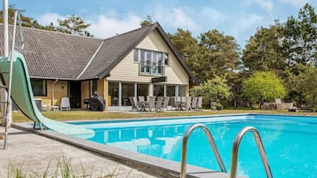 Uma piscina com escorregador, uma casa com varanda e mobiliário de exterior.